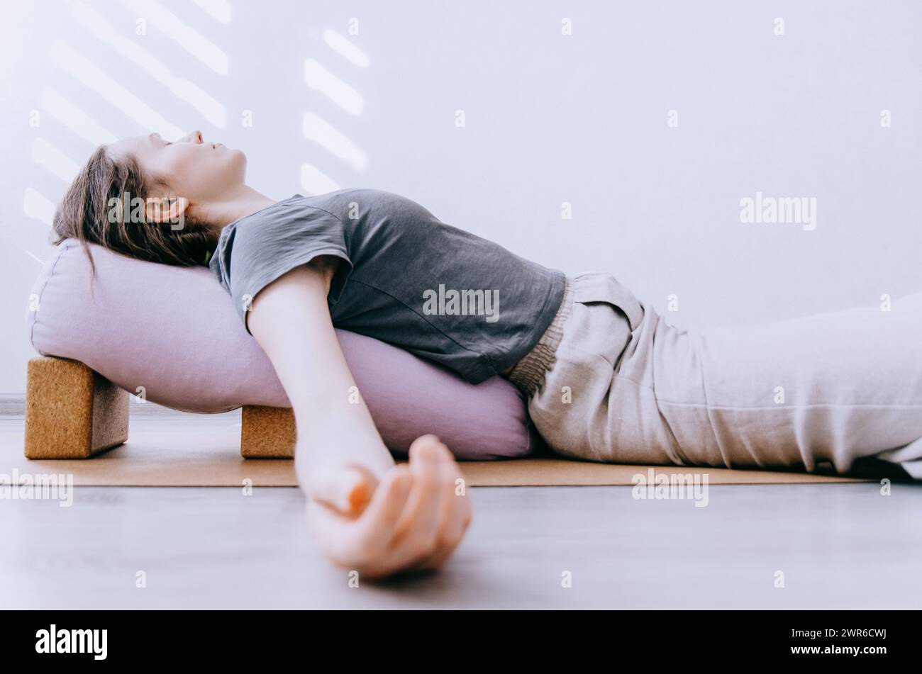 Woman in casual clothing doing yin/restorative yoga with bolster ...