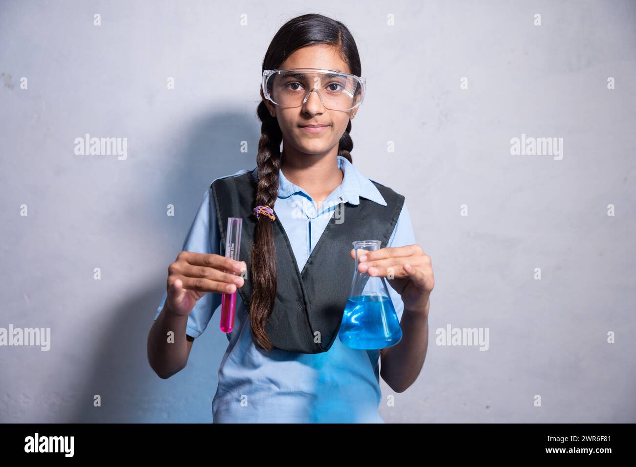 Happy Young Indian girl in school uniform wearing safety lab goggles ...