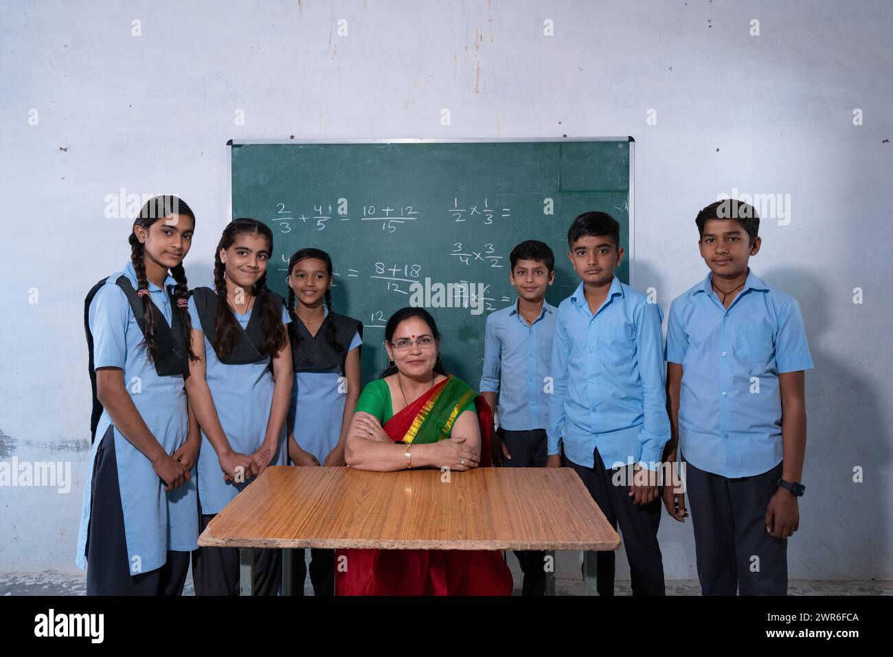 indian female teacher sitting in her classroom with Group of school kids in uniform looking at ...