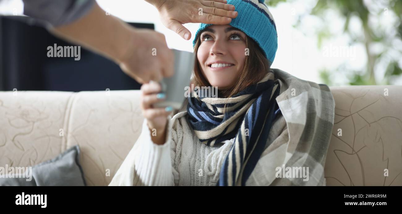 Man hand touching forehead of sick woman in hat and giving cup of tea ...