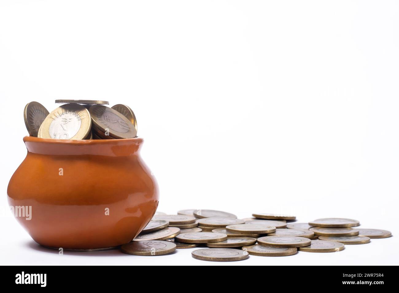 Coins of India in a clay pot and scattered on its side on a white ...