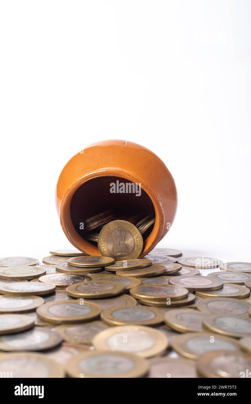 Indian coins spilling out of a clay pot isolated on white background ...