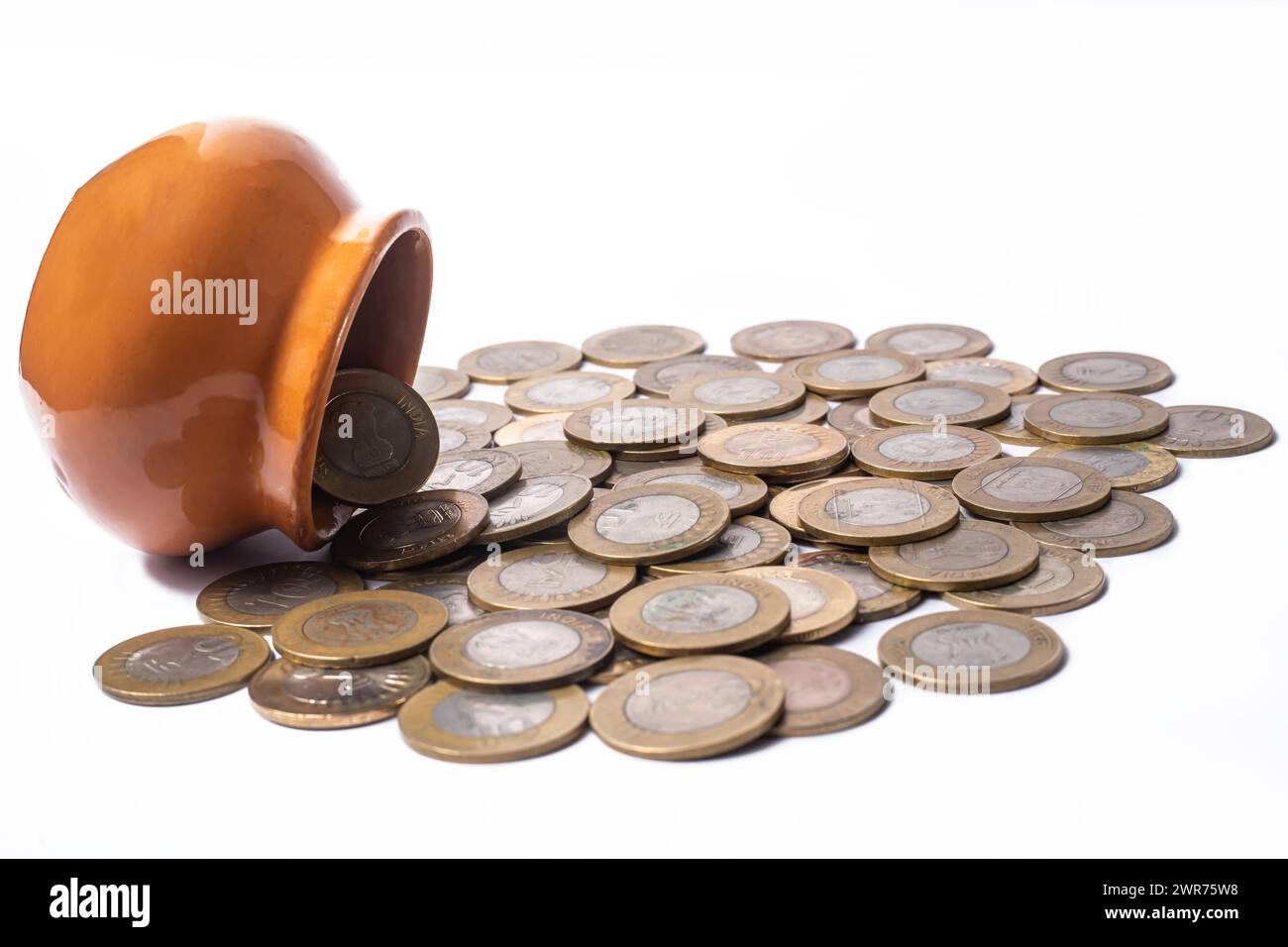 Various indian coins falling out of a tilting clay pot are scattered on ...
