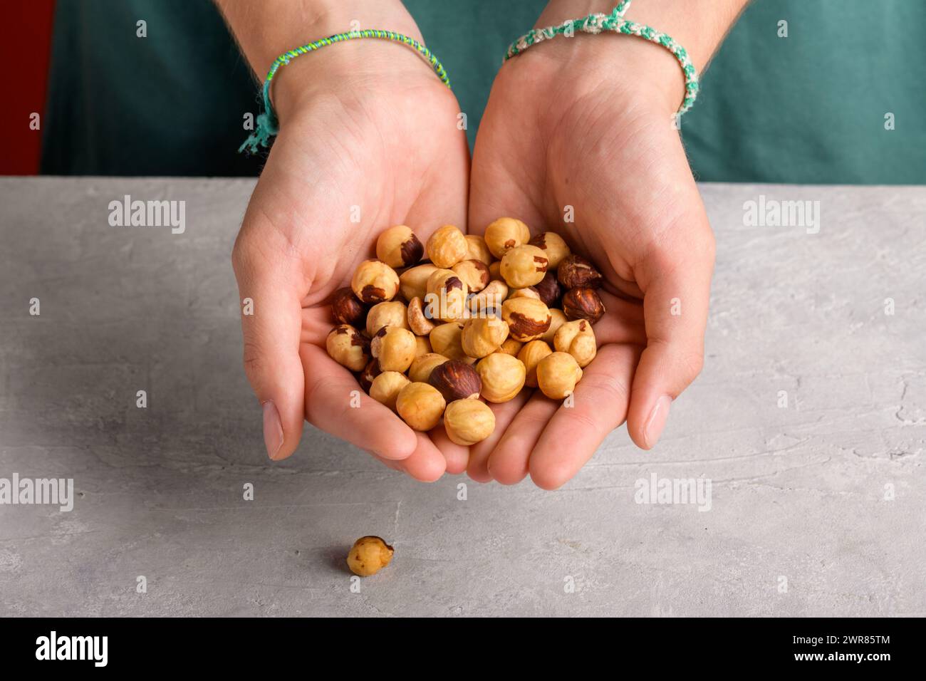 Woman holding peeled whole hazelnuts in her hands at gray table ...