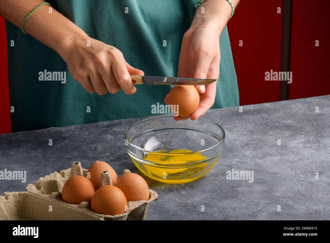 A woman's hand cracking an egg with knife into a clear glass bowl in ...