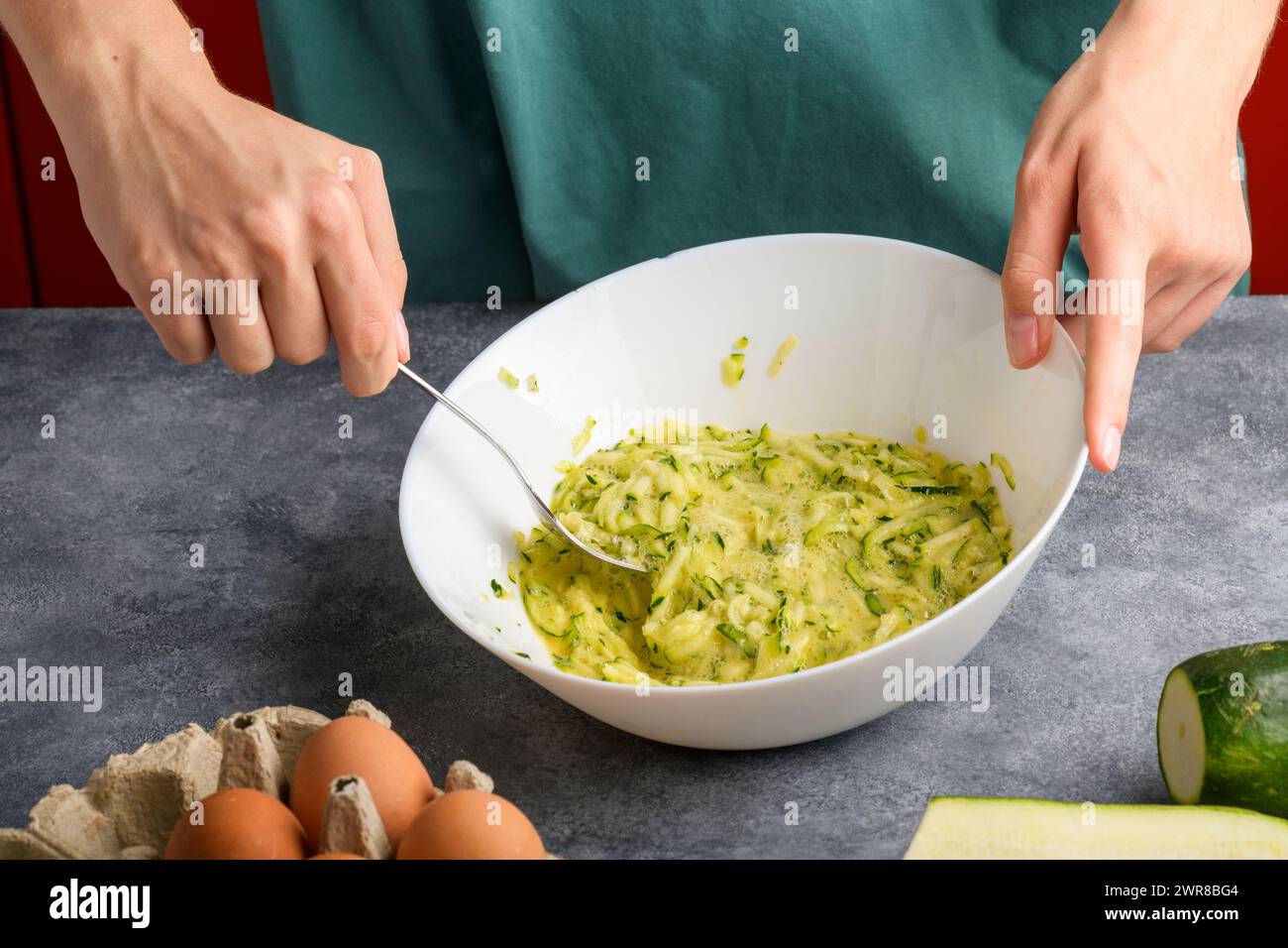 Female hands mixing with fork beaten eggs and grated zucchini in a ...