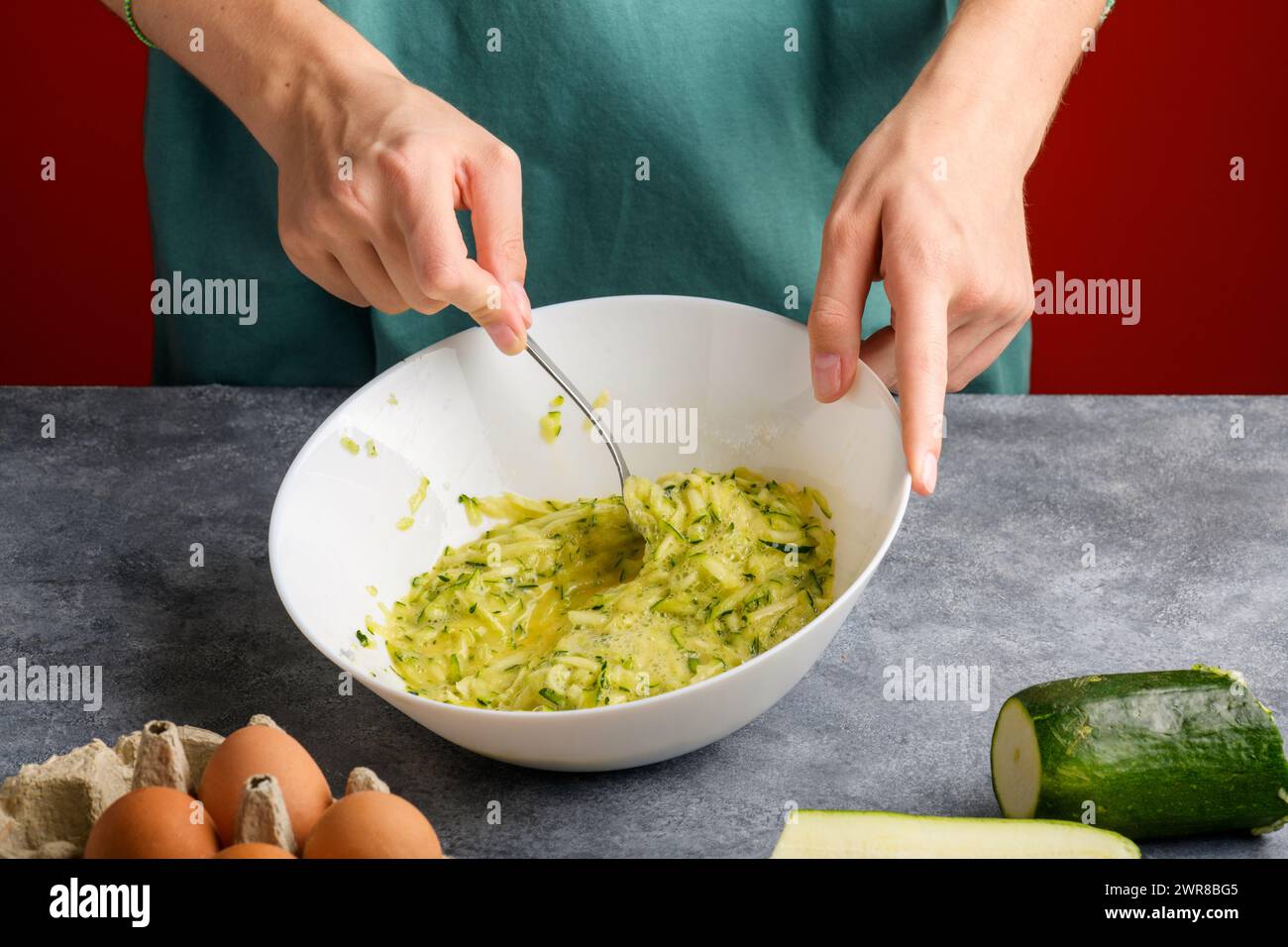 Female hands mixing with fork beaten eggs and grated zucchini in a ...