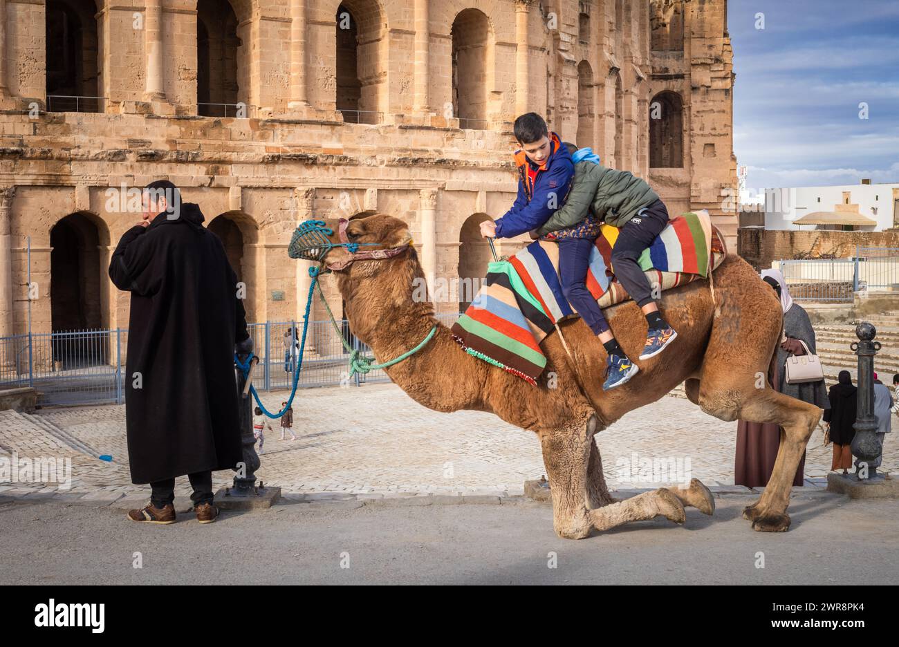 Two young boys have a camel ride outside well-preserved Roman El Jem ...