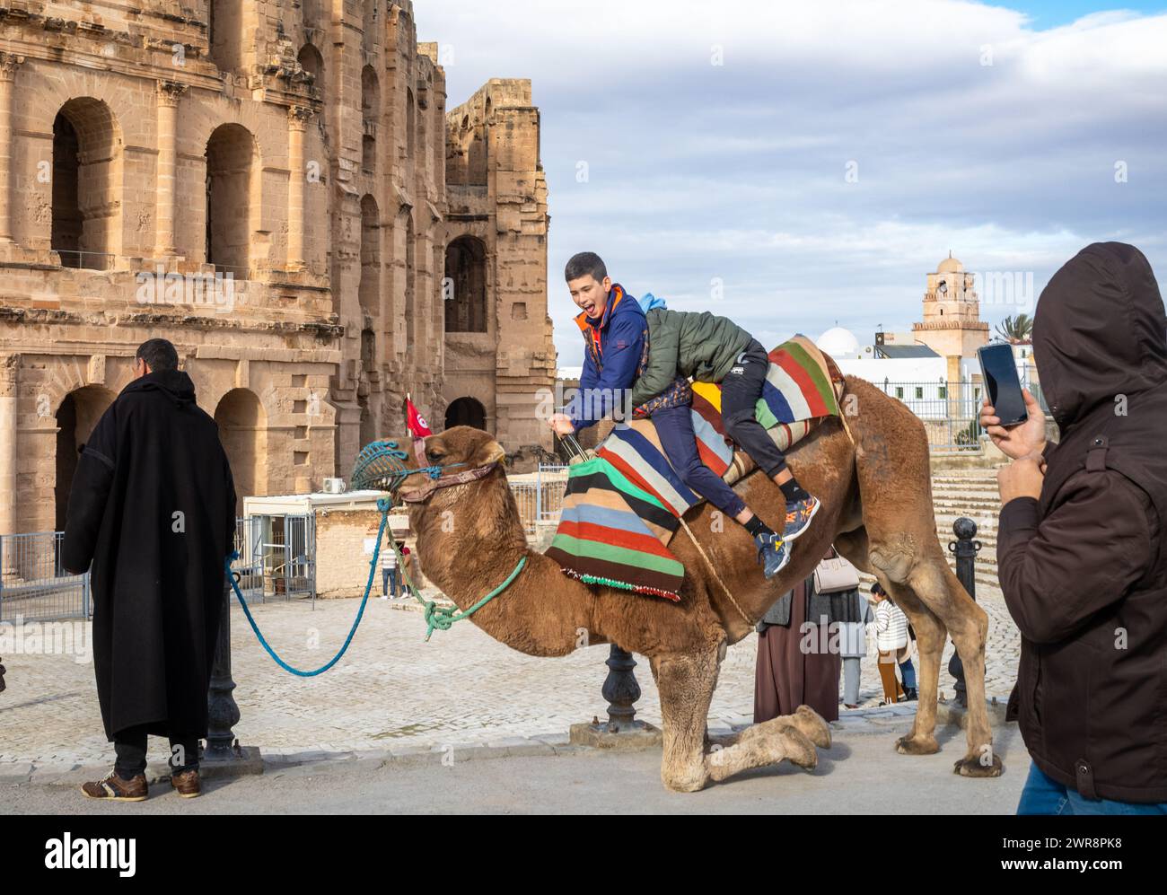Two young boys have a camel ride outside well-preserved Roman El Jem ...