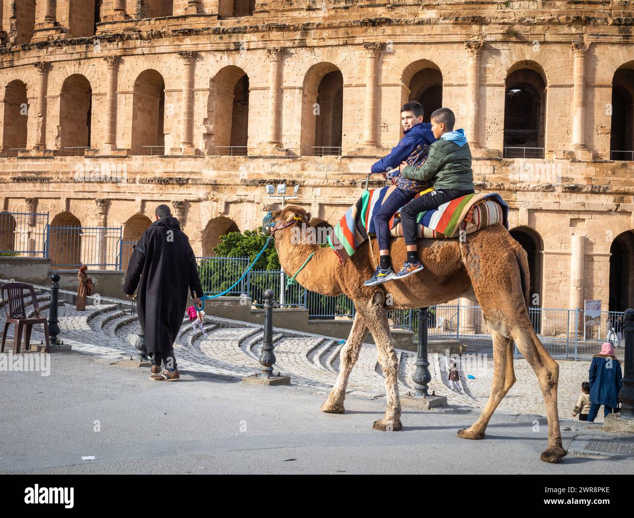 Two young boys have a camel ride outside well-preserved Roman El Jem ...