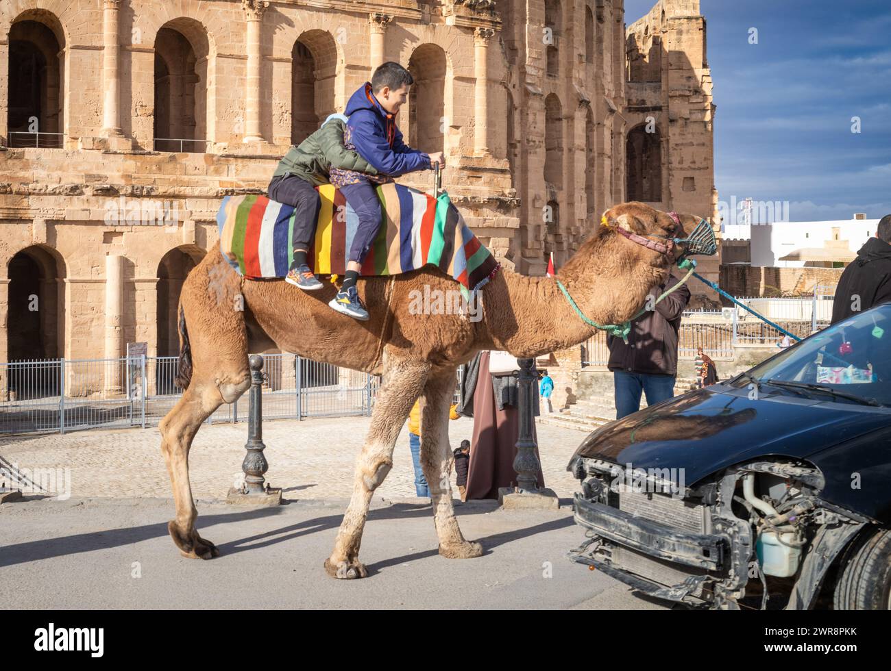 Two young boys have a camel ride outside well-preserved Roman El Jem ...