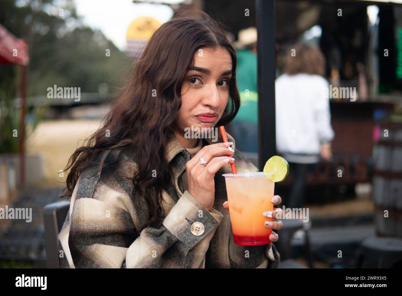 A young Latina woman with a playful expression sips a colorful cocktail ...