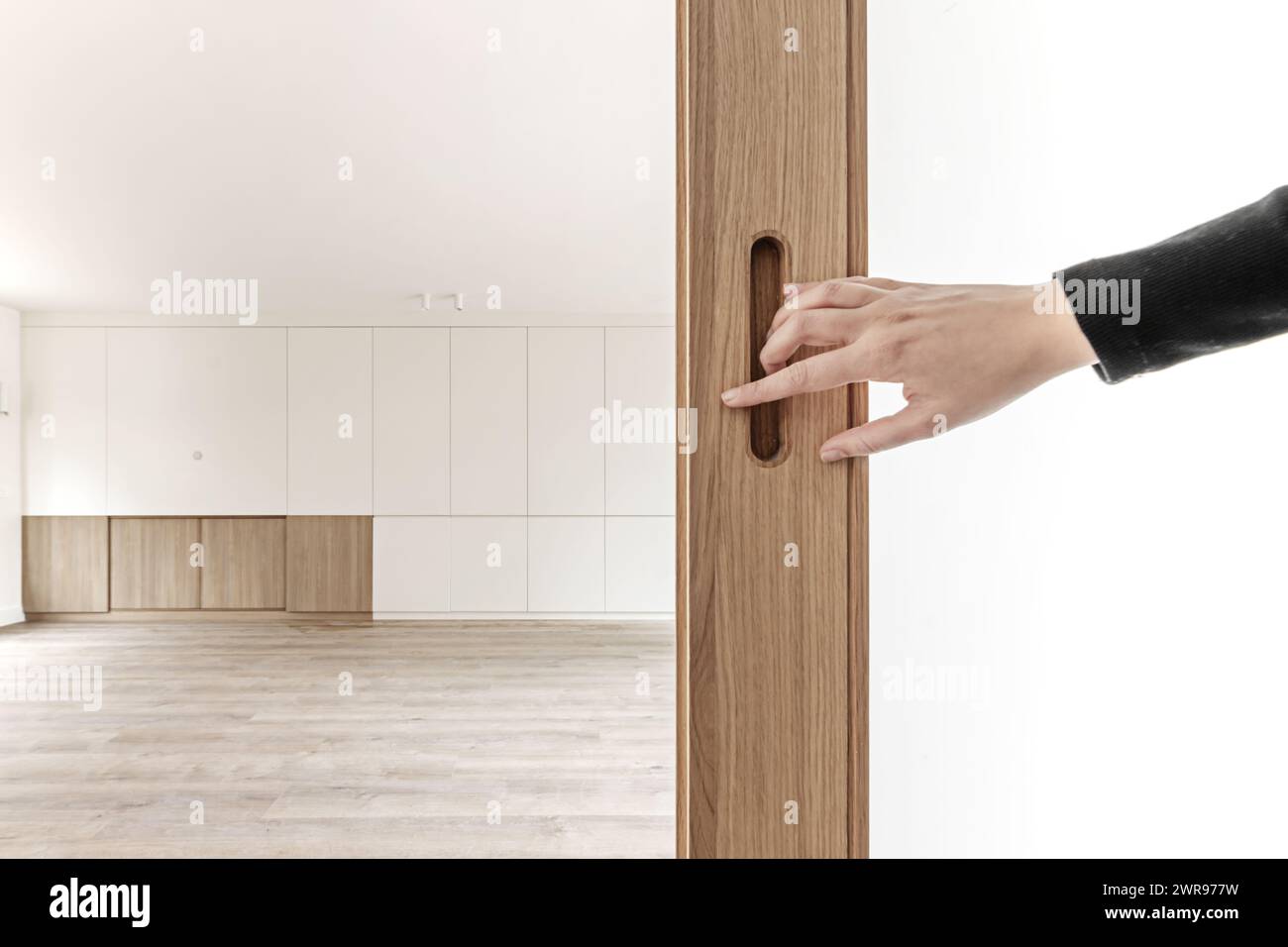 A hand opening a door to an empty living room of a multi-story detached ...