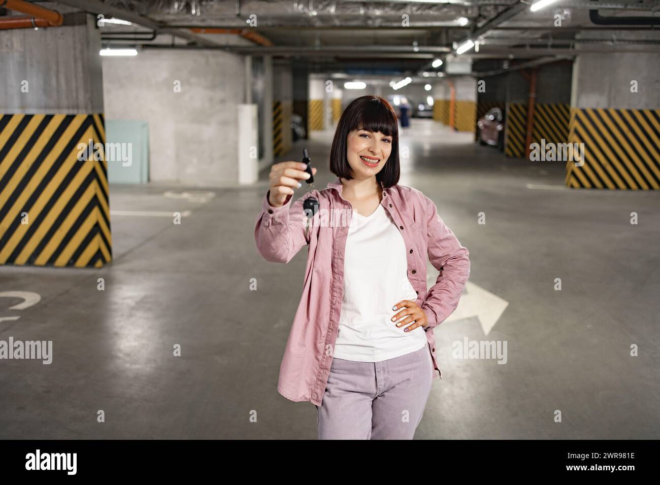 Woman standing in underground parking lot in casual clothes holding ...