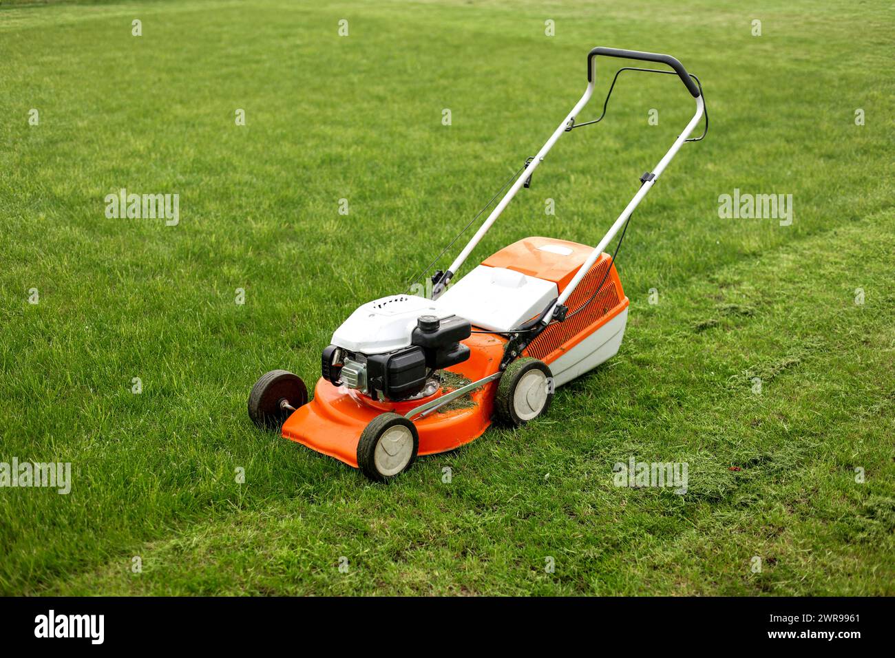 Top view of modern orange-grey gasoline lawn mower cutting bright lush ...