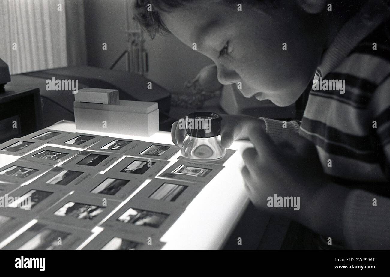 1960s, historical, a young boy using a magnifier loupe to look at some ...