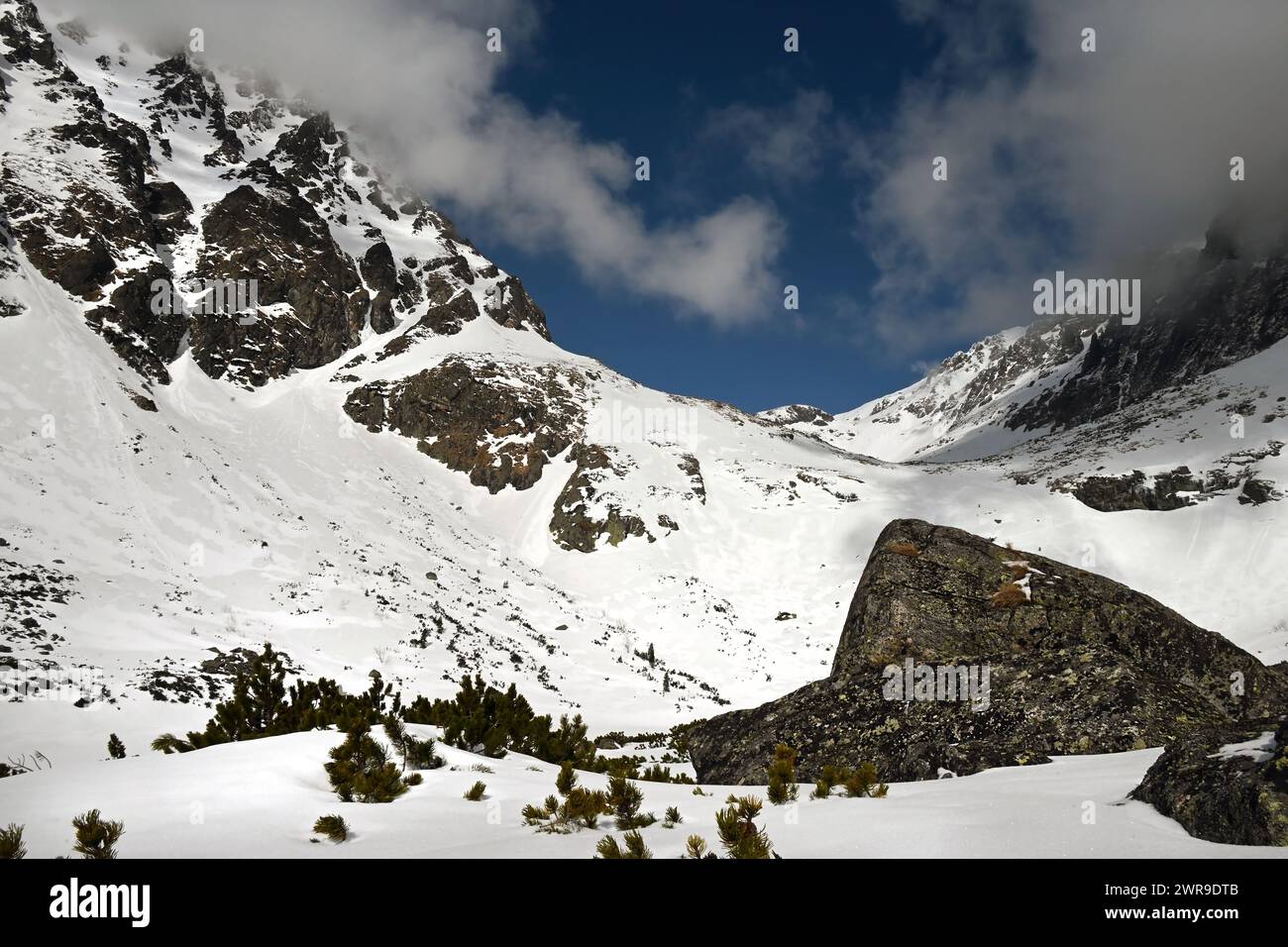 Rock, snow-covered mountains under blue sky and clouds near Velické ...