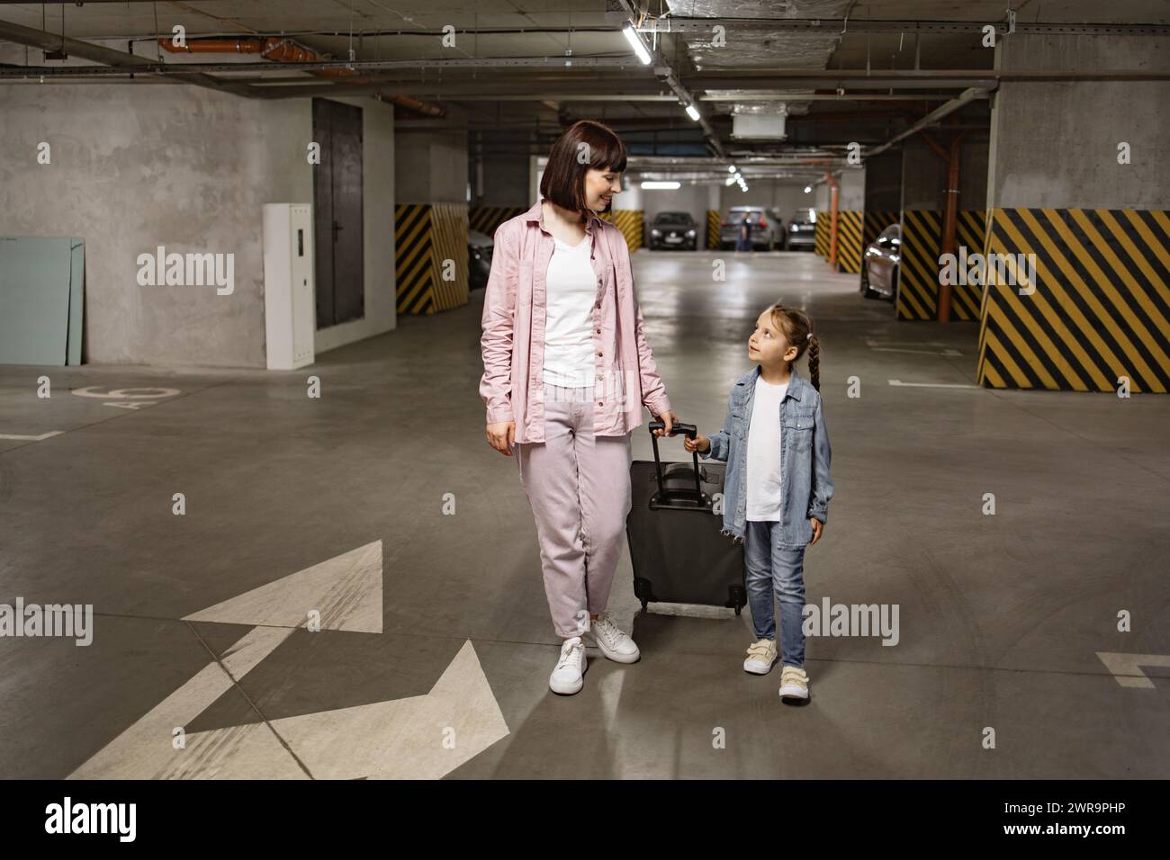 Happy mom and small daughter stroll through subterranean parking area ...