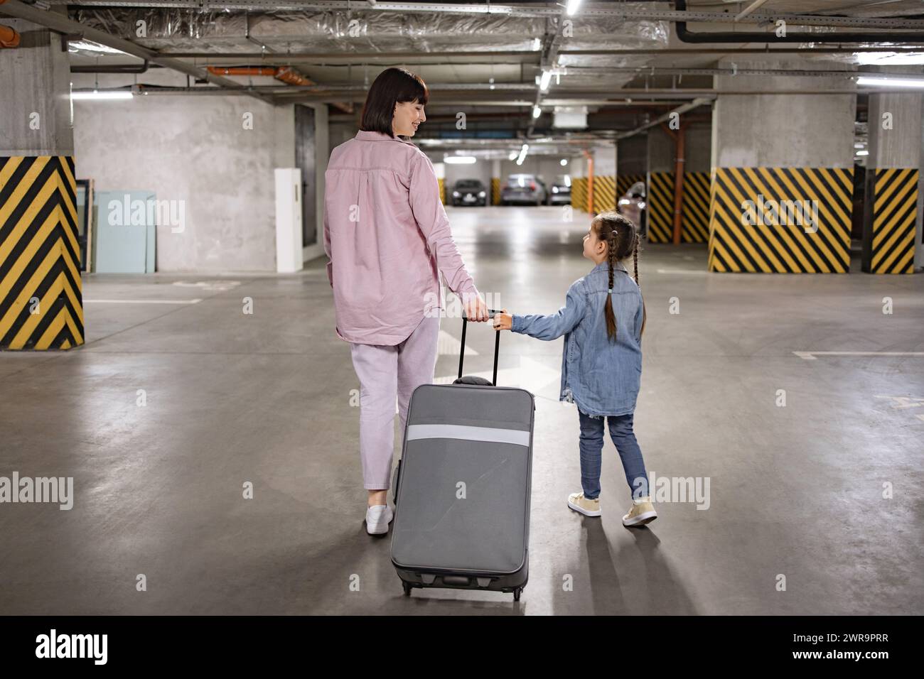 Happy mom and small daughter stroll through subterranean parking area ...