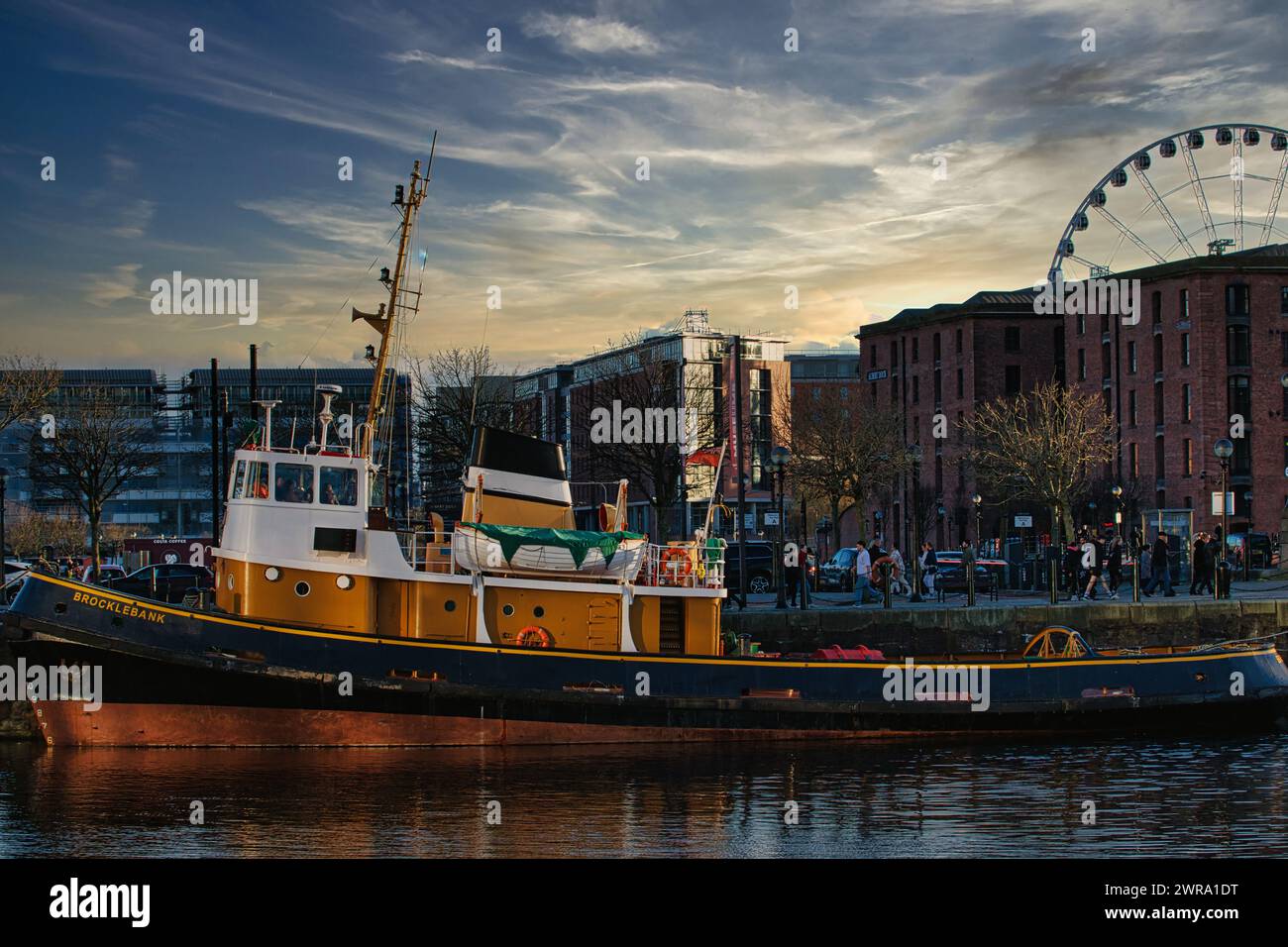 Tugboat in city harbor at sunset with ferris wheel and buildings in ...