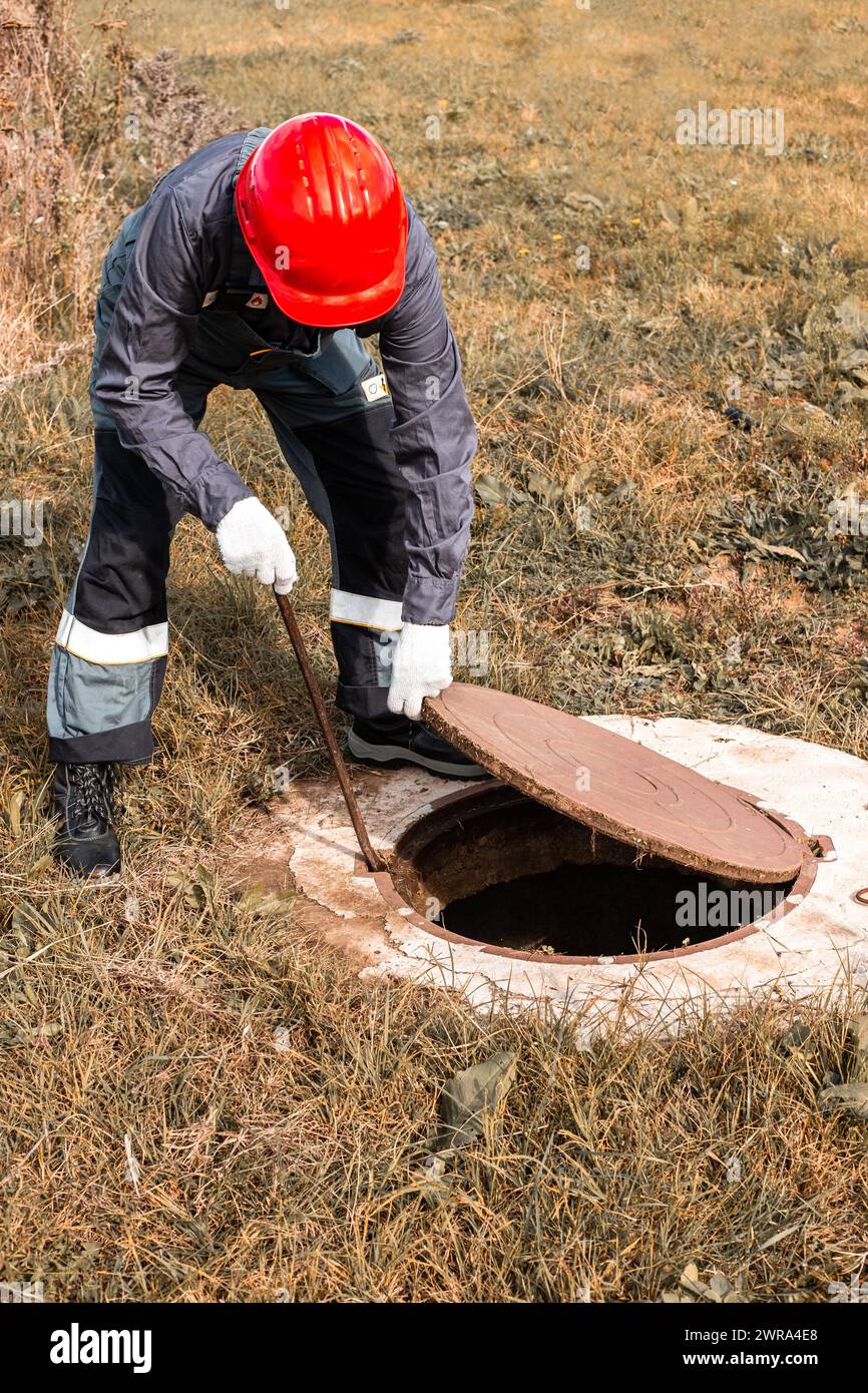 A worker in a hard hat lifts a manhole cover on a septic well ...