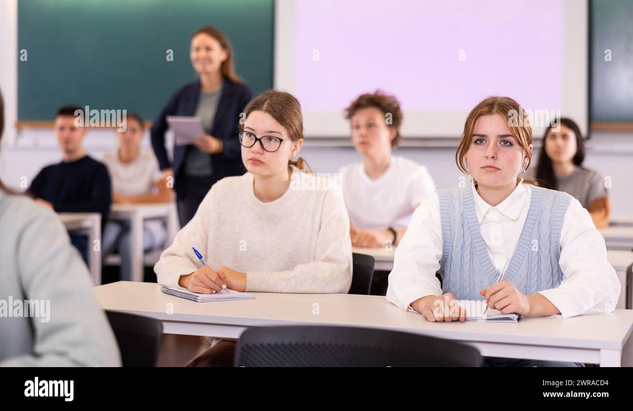 Group of school teenagers with pens and notebooks studying in classroom ...