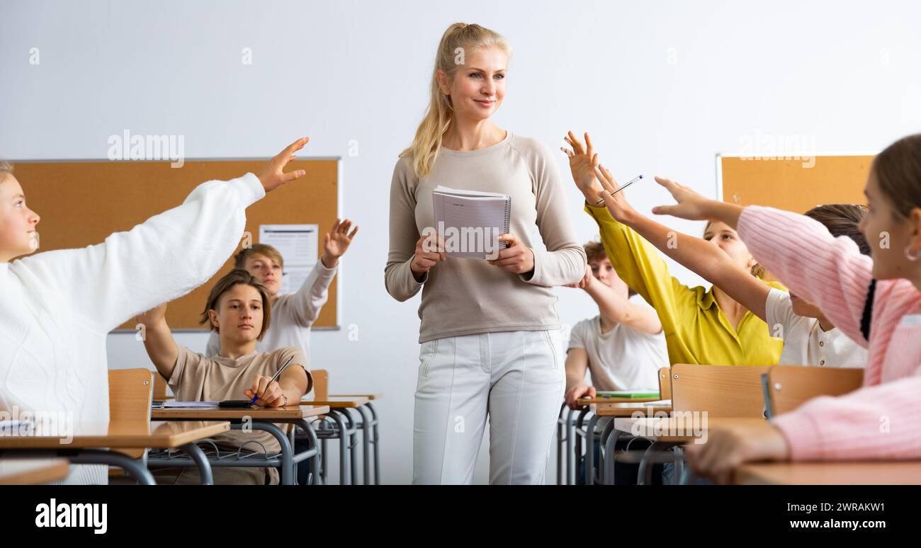 Female teacher lecturing in classroom and kids raising hands Stock ...