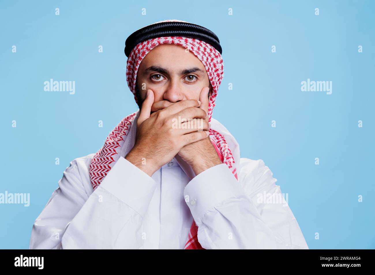 Man wearing traditional islamic clothes covering mouth with hands ...