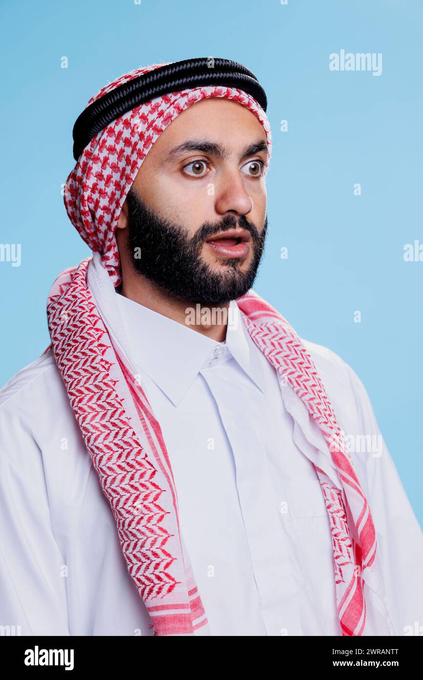 Shocked muslim man dressed in traditional headscarf looking away with ...