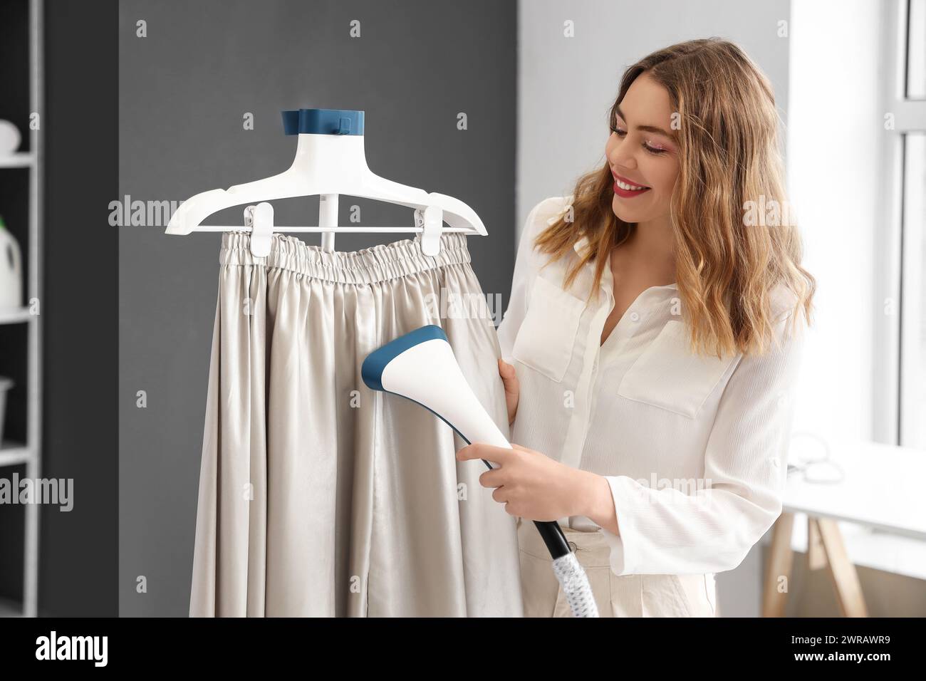 Pretty young woman steaming clothes with modern garment steamer in ...