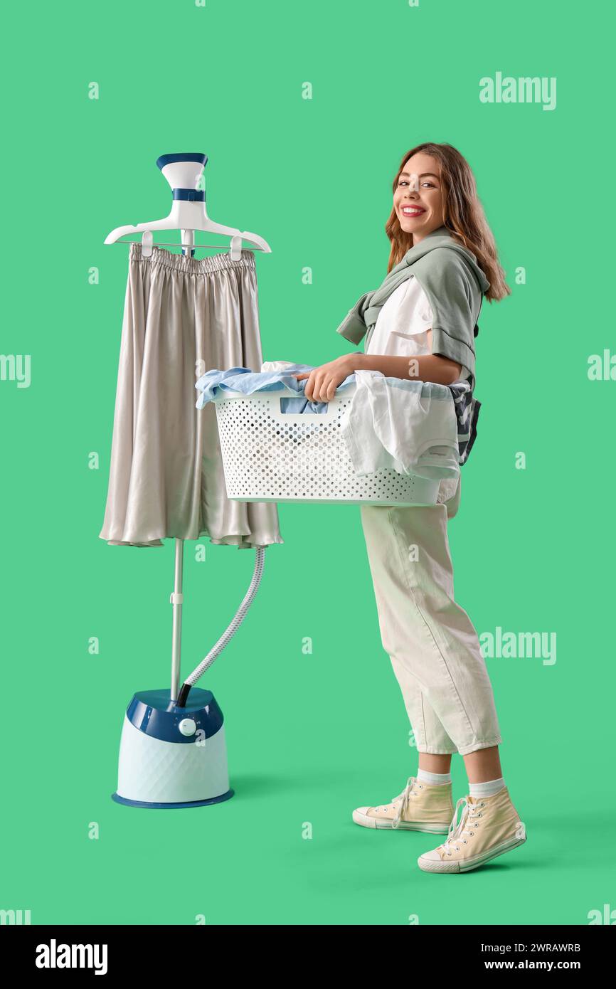 Pretty young woman with modern garment steamer and basket full of ...