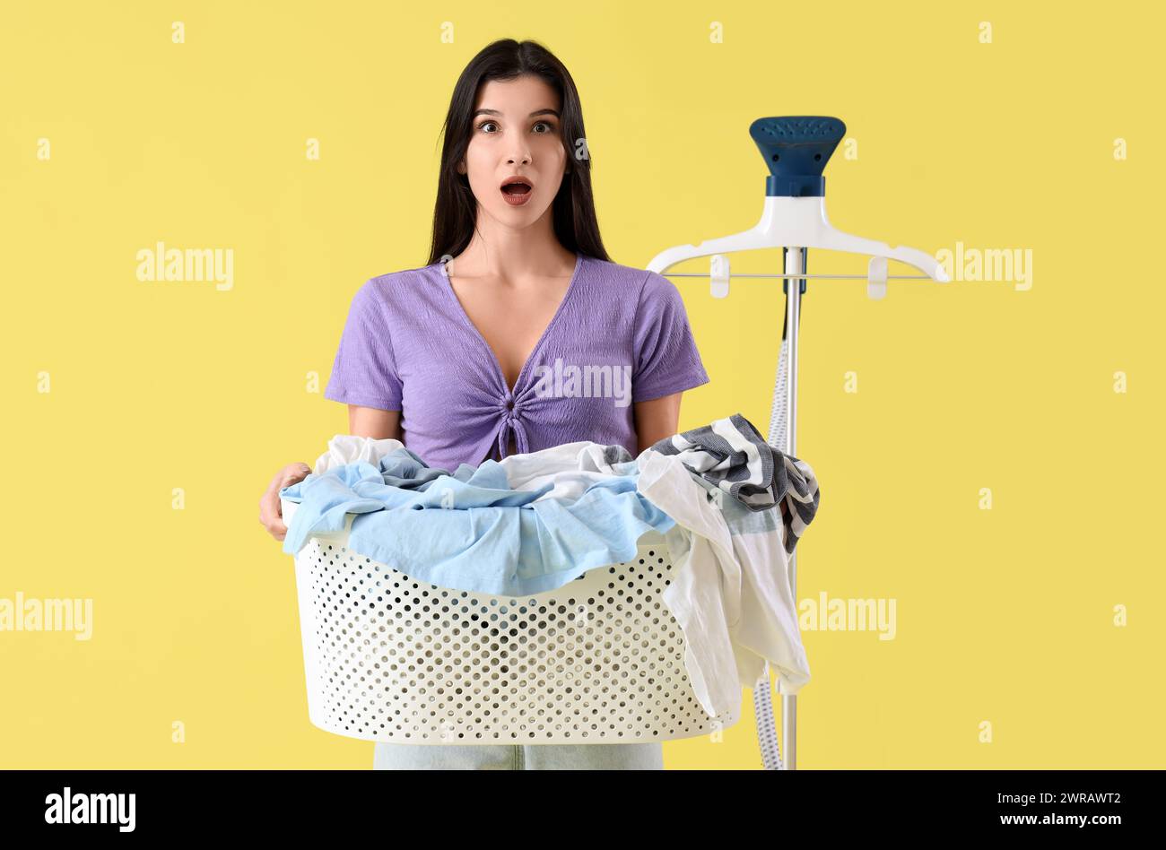Shocked young woman with modern garment steamer and basket full of ...