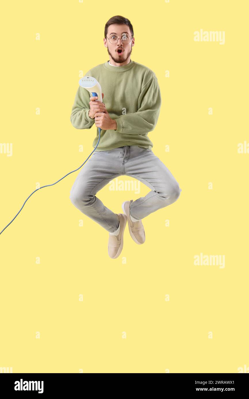 Shocked young man with modern steamer jumping on yellow background ...