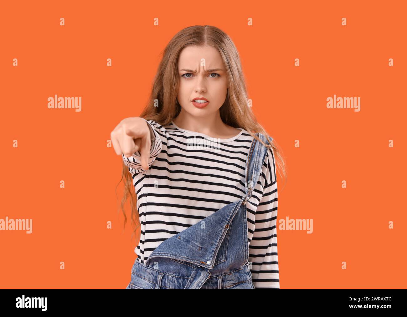 Young woman pointing at viewer on orange background. Accusation concept ...