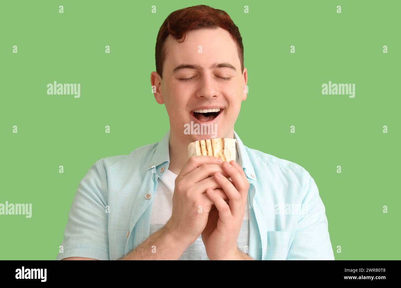 Young happy man eating doner kebab on green background Stock Photo - Alamy
