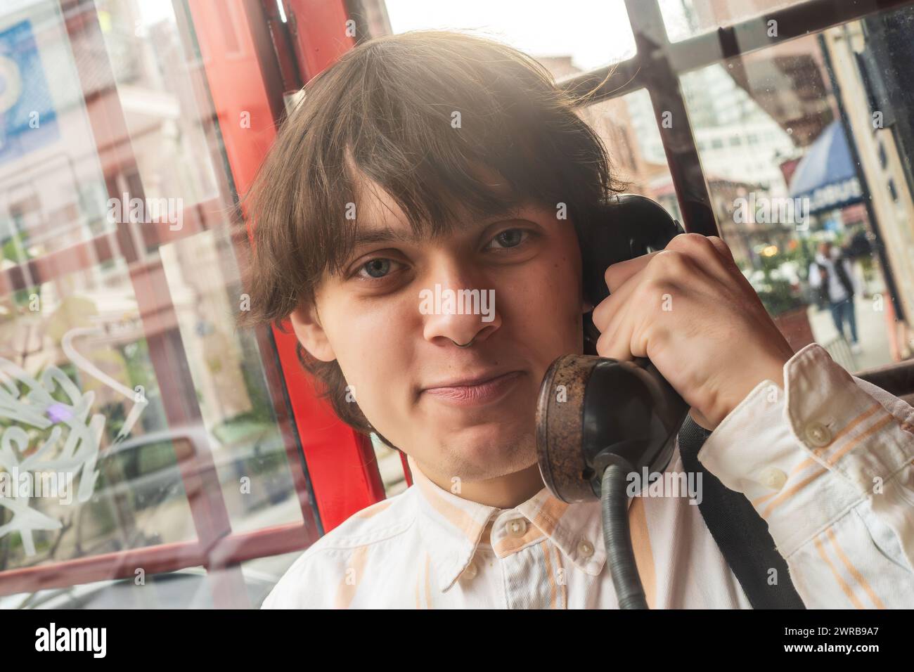 Cheerful young man smiles while making call in classic red telephone ...