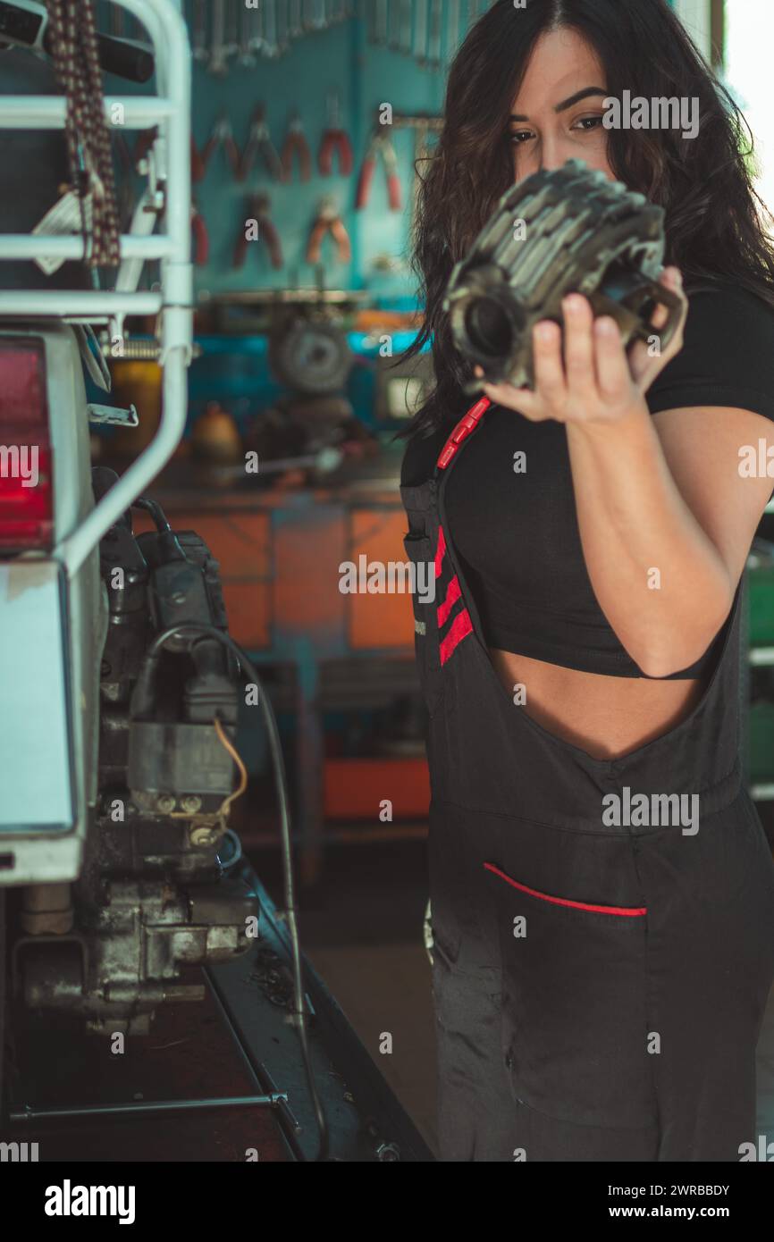 Professional latino female motorbike mechanic holding component of ...