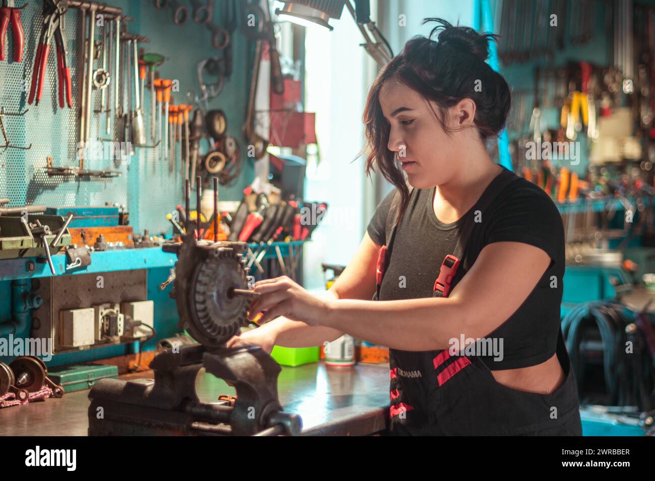 A woman is attentively working on a mechanical piece at a tidy workshop ...