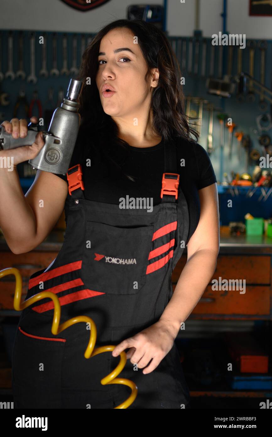 Playful hispanic female mechanic making a gesture in the workshop, a ...