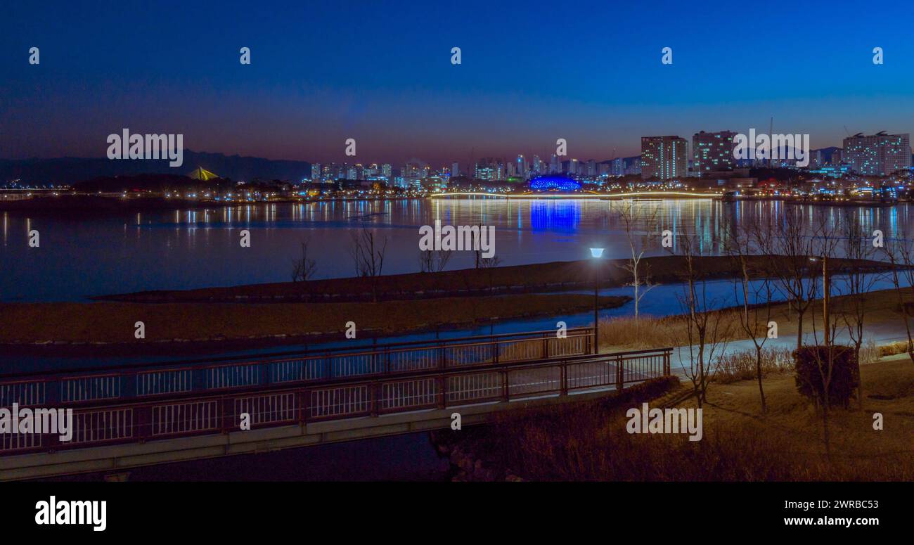 Night view of a lit pathway along a tranquil urban riverside with city ...