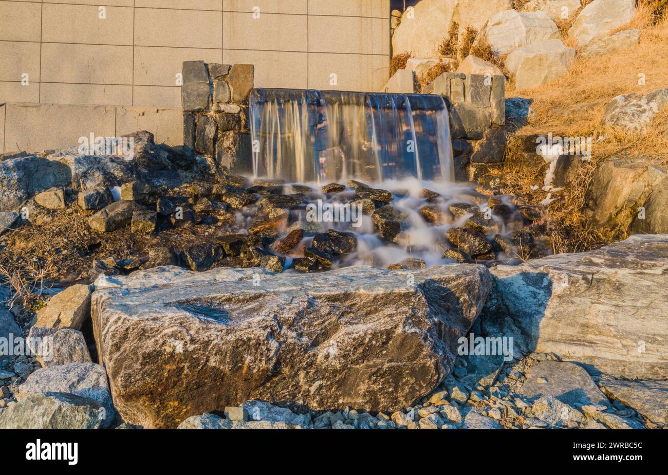 A man-made waterfall flows gently over sunlit rocks, in South Korea ...