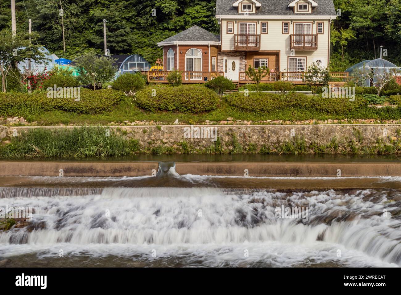 Elegant houses overlook a small cascading waterfall on the riverbank ...