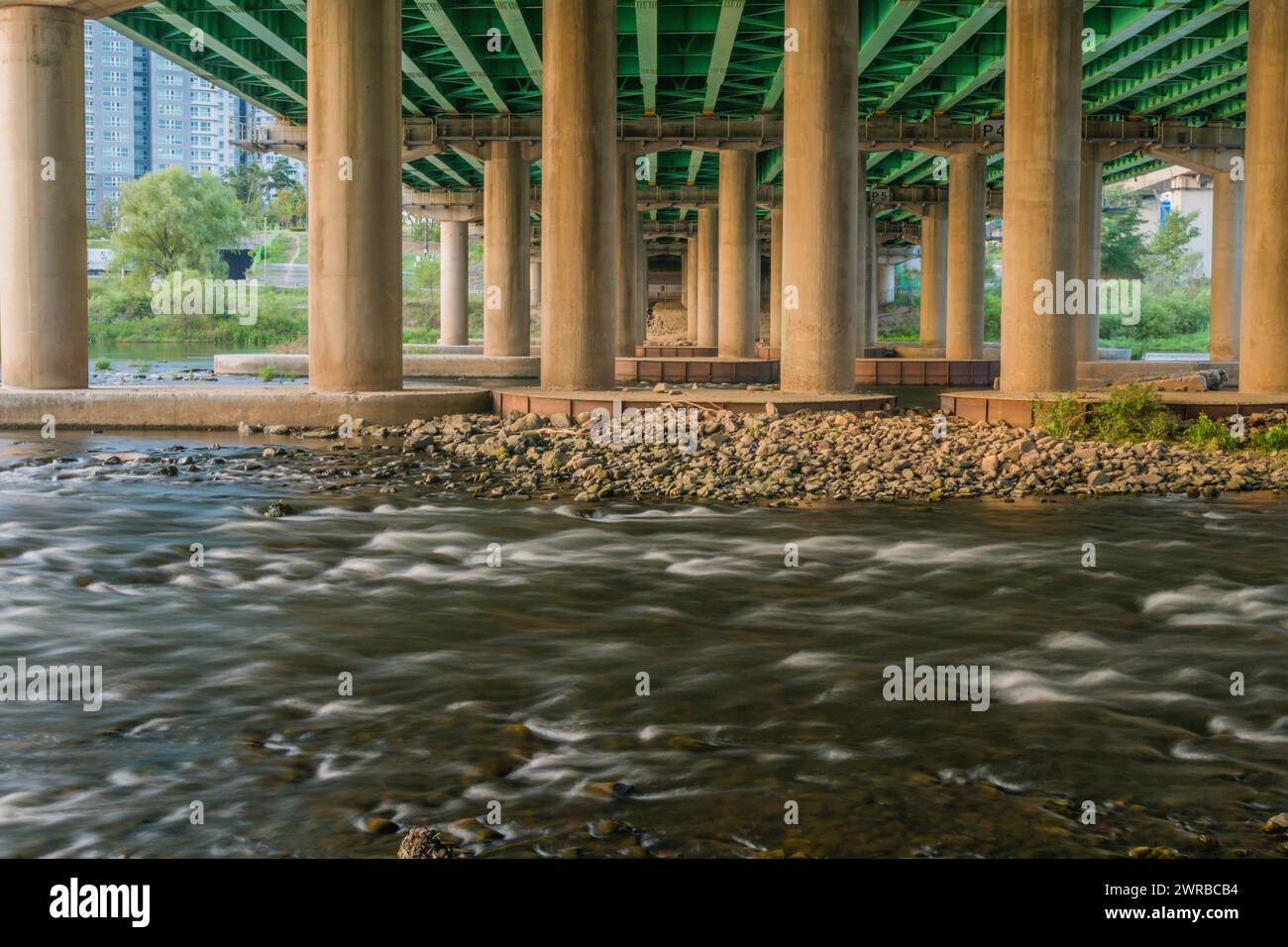 Long exposure shot of a river flowing under a green bridge with columns ...