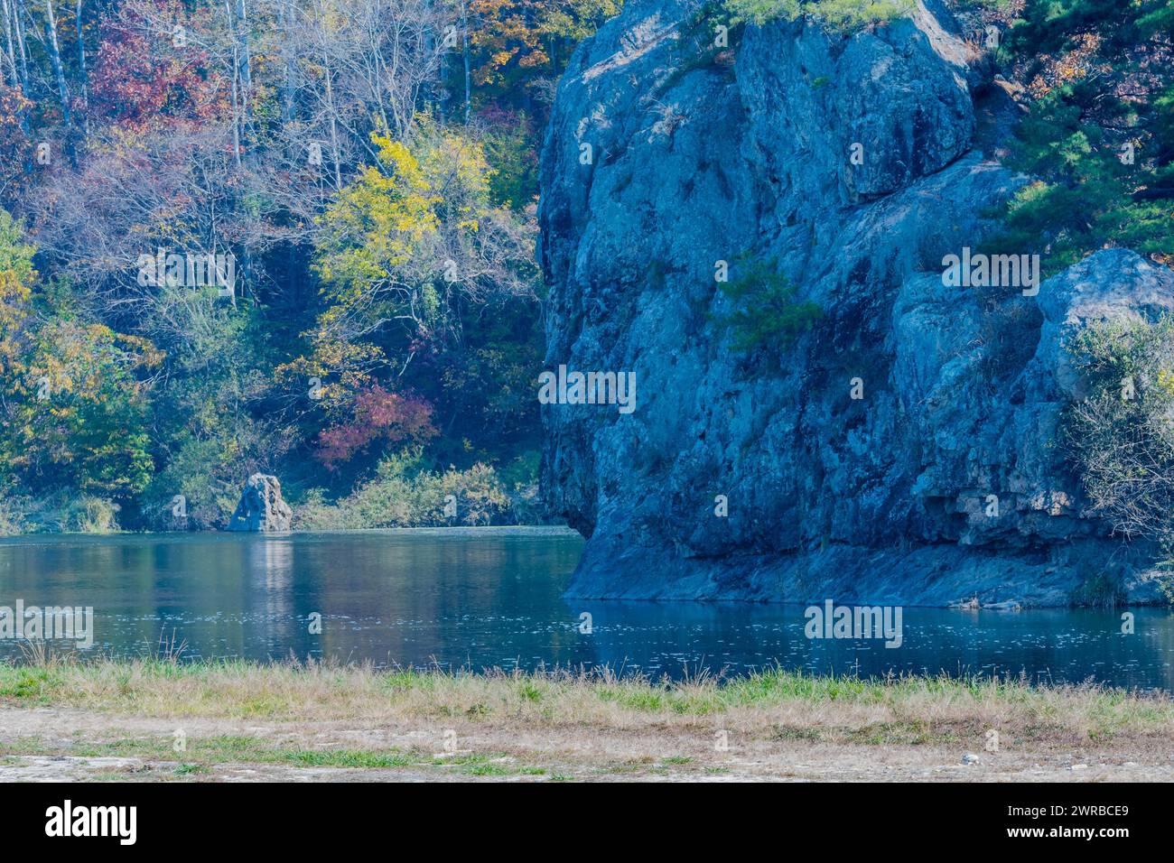Rock faces with autumnal trees reflected in a calm lake creating a ...