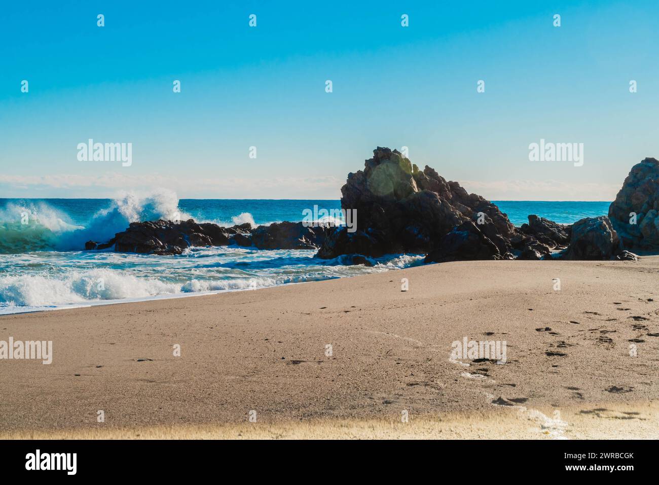 Gentle waves meet the sandy beach with prominent rocks and clear blue ...