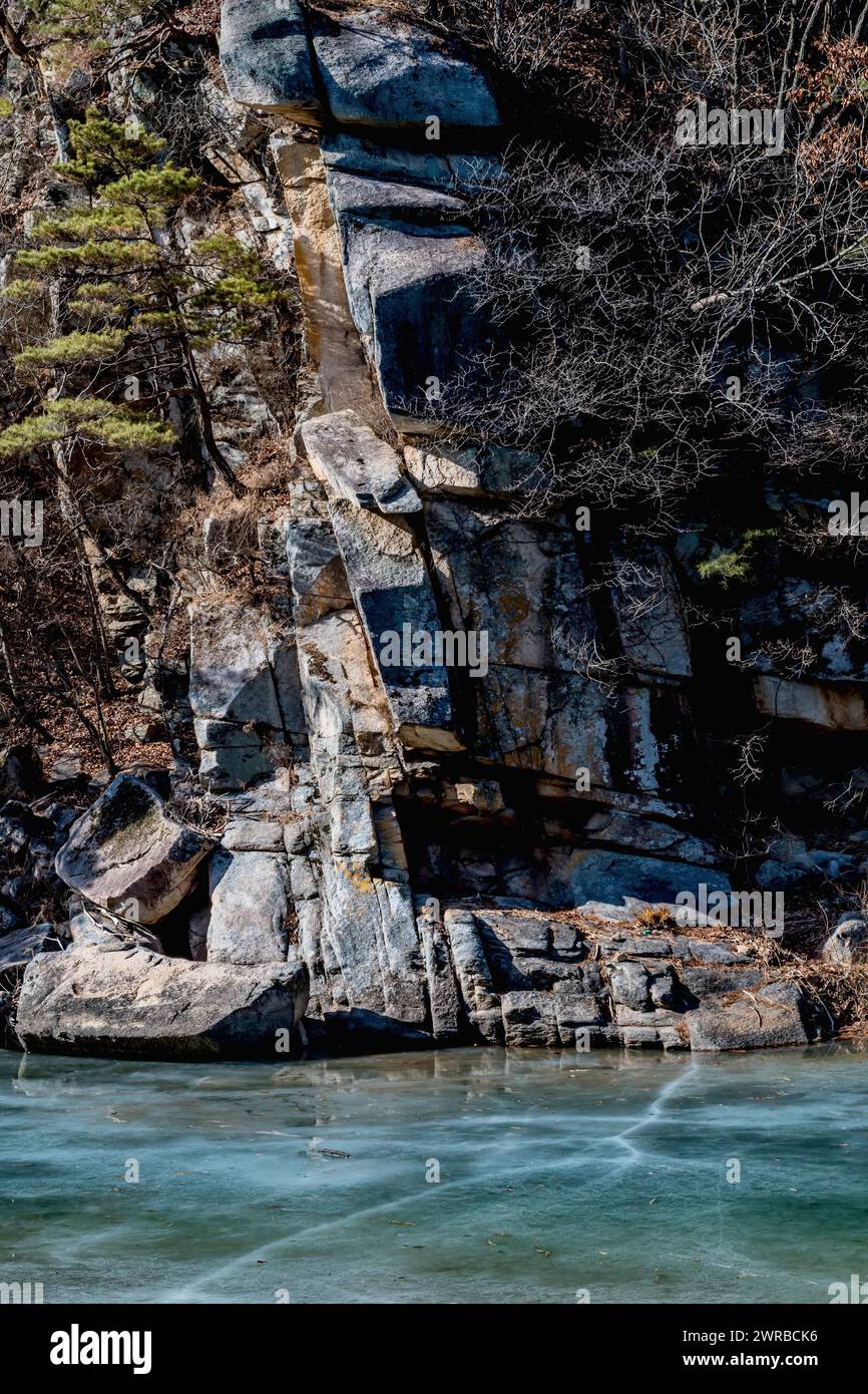 Sunlight casting shadows on a rocky cliff above a frozen river lined ...
