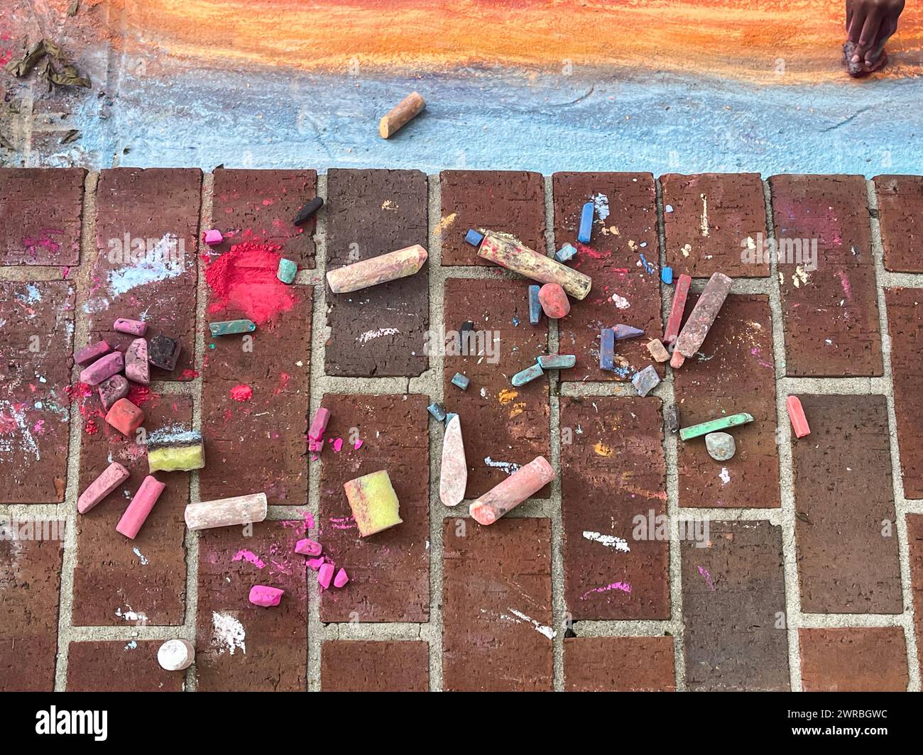 A child's hand uses loose chalk to draw an image on the sidewalk at a ...