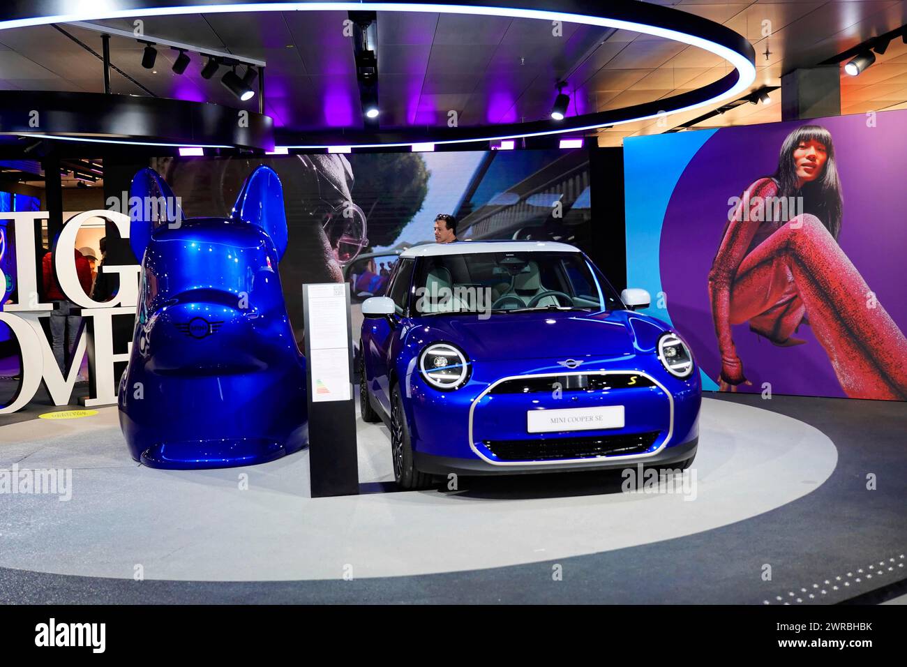 A blue Mini Cooper is presented at a car show next to a large model ...