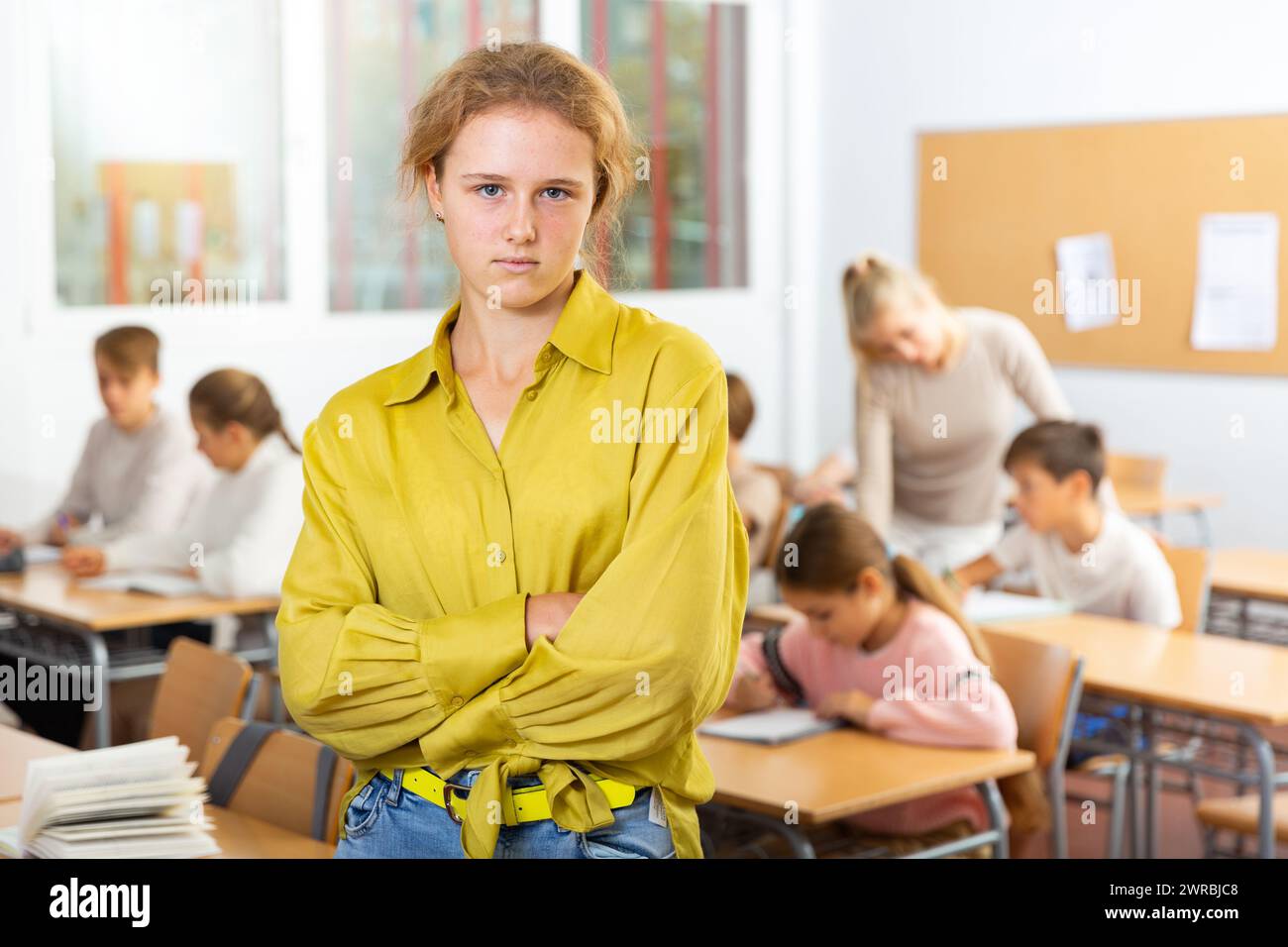 Upset girl stands in a school class against background of classmates ...