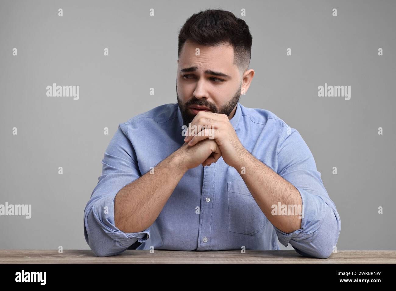 Portrait of sad man at wooden table on light grey background Stock ...